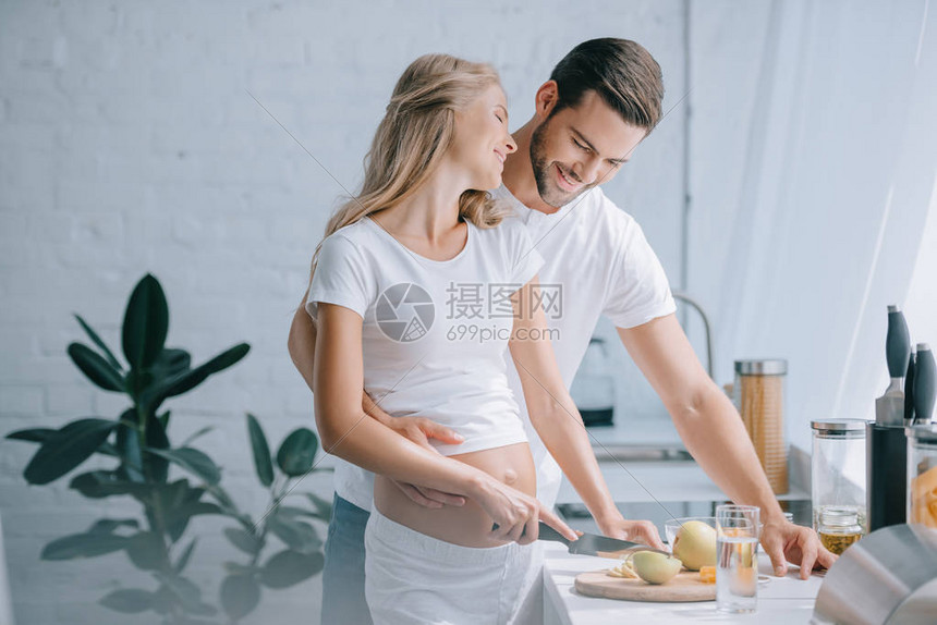 幸福的孕妇和丈夫在家里一起烹饪水果沙拉高清图片下载-正版图片502706459-摄图网