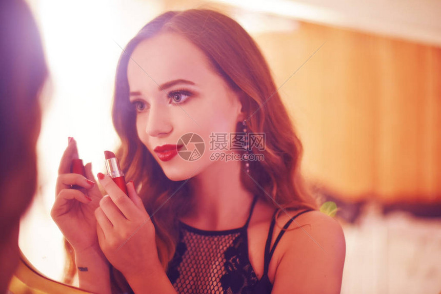 一个美丽的年轻女子正在做自己的改造用红光在镜子前用口红做晚妆的cerly头发的女孩关高清图片下载-正版图片502958237-摄图网