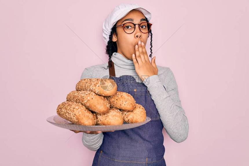 年轻的非洲裔美国面包师妇女穿着围裙拿着全麦面包和麦片盖嘴用手震惊地为错误感到羞耻高清图片下载-正版图片503869232-摄图网