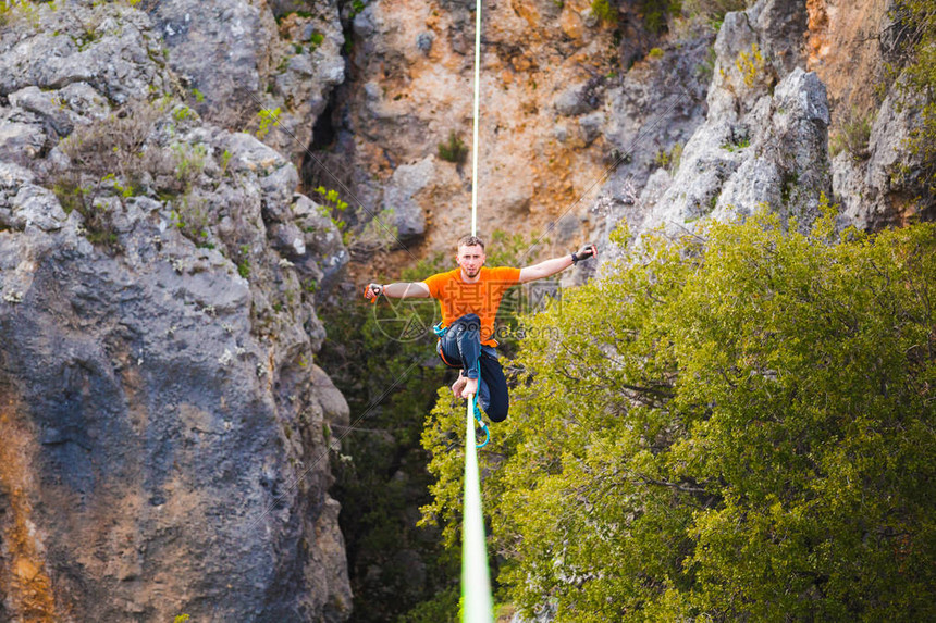 高线山脉的背景一个人坐在拉长的吊索上走钢丝的表演Highliner在深渊上保持平衡运动员摔倒高清图片下载-正版图片504528904-摄图网
