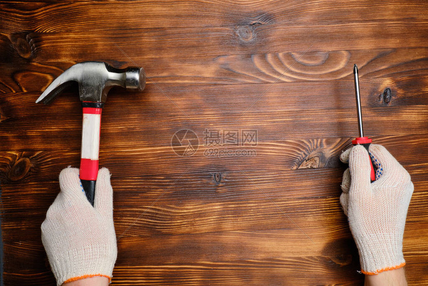 戴着工作破布手套的手在木质背景上握着一把锤子和一把螺丝刀高清图片下载-正版图片504540832-摄图网