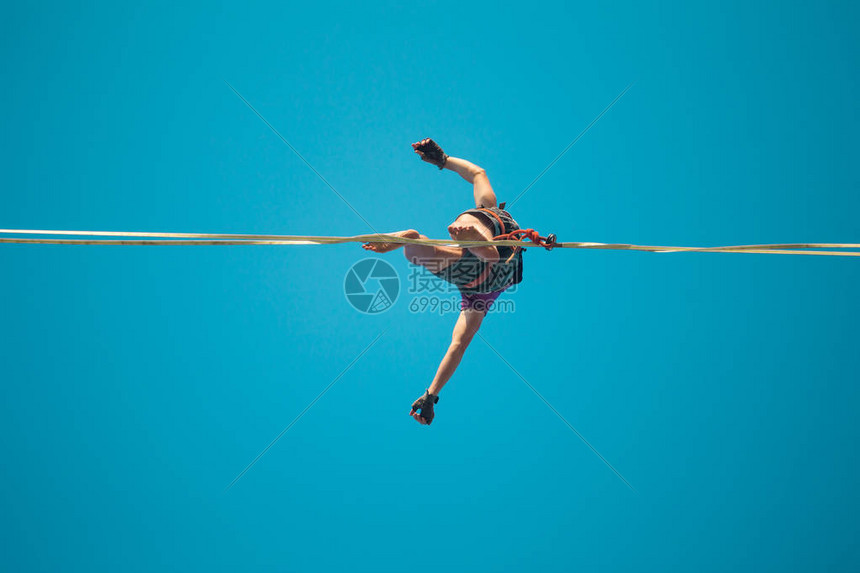 以蓝天为背景的Highliner做出了动作一个男人从下面沿着伸展的吊索视图行走能走钢丝人在深渊中保持平衡向前迈出了高清图片下载-正版图片506160188-摄图网