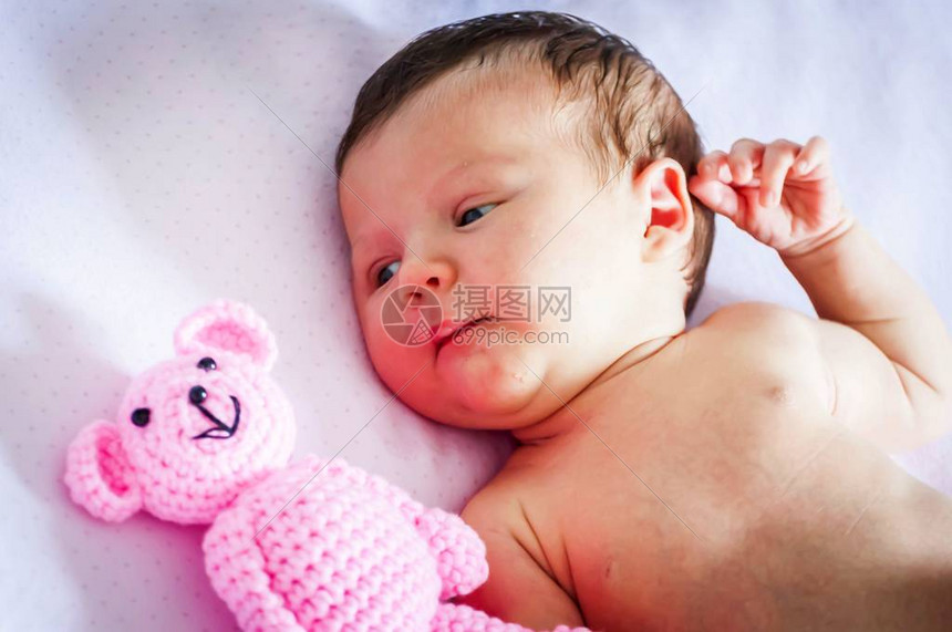 躺在摇篮里看着一只粉色泰迪熊的可爱新生女婴高清图片下载-正版图片507456312-摄图网