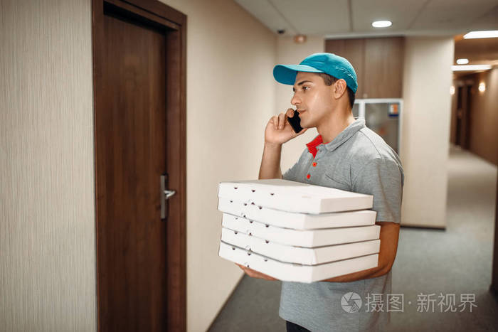 送披萨的人在门口打电话给客户送货服务。 皮兹里亚的快递员拿着纸箱,在室内通过电话交谈照片 正版商用图片15wkk4 摄图新视界
